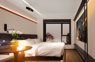 Quarto de hotel moderno com cama, mesa de cabeceira e uma janela grande.