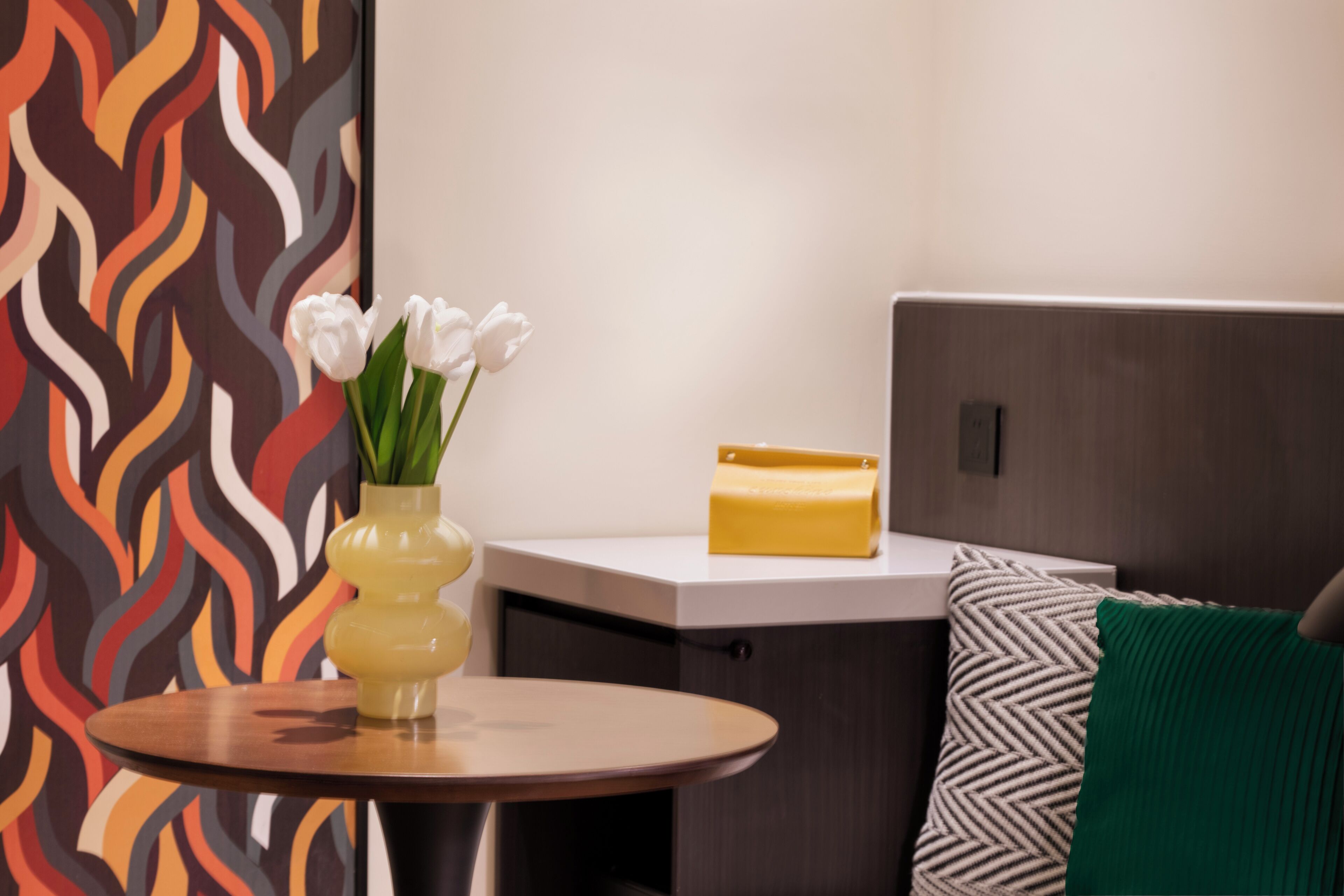 Quarto moderno com mesa redonda, um vaso com flores brancas, uma bolsa amarela e almofada estampada.