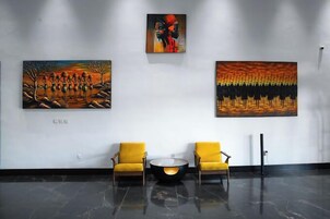 Um lobby com dois poltronas amarelas, uma mesa redonda e três obras de arte na parede.