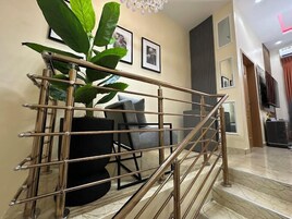 Uma escada com corrimão de metal, um vaso de planta, um sofá cinza e um quadro na parede.