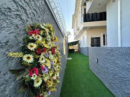 Um corredor estreito com gramado sintético verde e parede decorada com uma variedade de flores coloridas.