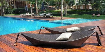 Uma área na beira da piscina com deck de madeira, espreguiçadeiras e piscina.