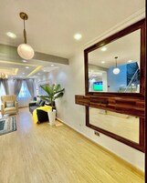 Uma sala de estar espaçosa com um espelho grande, piso de madeira, um sofá, uma poltrona e um vaso de planta.