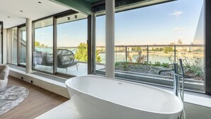 Uma casa de banho moderna com uma banheira independente, grandes janelas e vista para um rio e horizonte urbano.
