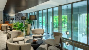 Um lobby de hotel moderno com grandes janelas de vidro, assentos confortáveis e uma planta central.