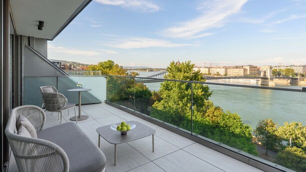 Varanda com vista para um rio e uma ponte, mobiliada com cadeiras e mesa.