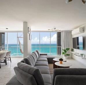 Uma sala de estar moderna com um sofá grande, uma área de jantar e uma varanda com vista para o oceano.