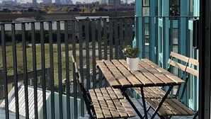 Uma varanda com mesa e banco de madeira, um vaso de planta e vista para a cidade ao fundo.