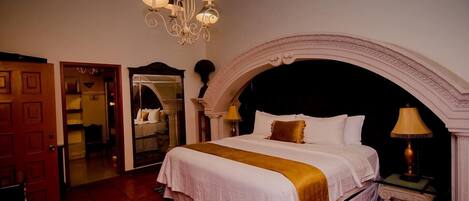 Quarto com cama grande, lustre, espelho e porta que dá para outro cômodo.