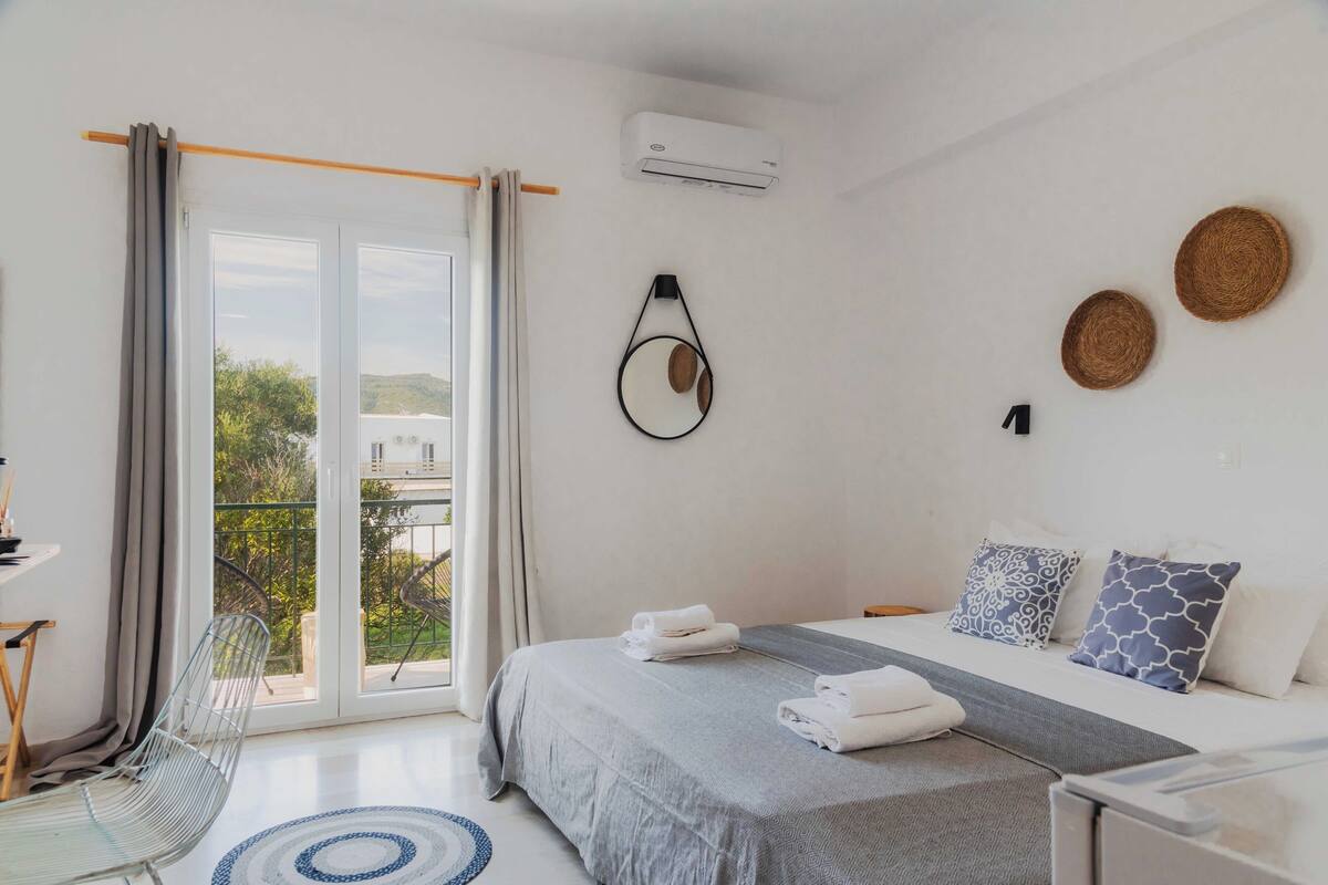 Quarto com cama, poltrona, escrivaninha, vista para a varanda e ar condicionado.