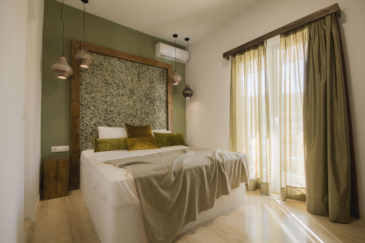 Quarto com cama, cabeceira com padrão texturizado, piso de madeira e janela com cortinas.