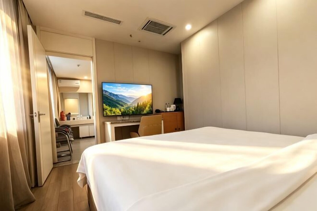 Quarto de hotel com uma cama, uma escrivaninha com televisão e uma cozinha compacta.