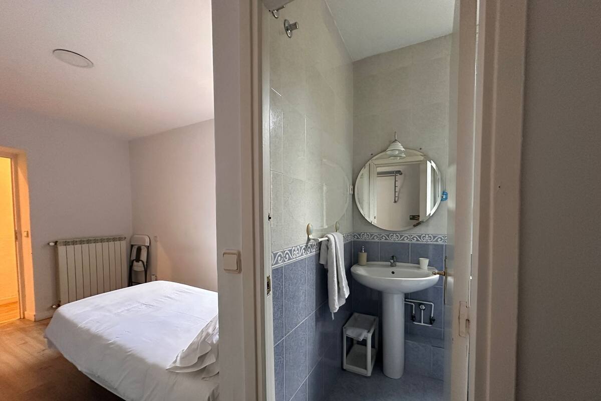 Quarto de hotel com cama, banheiro com pia e espelho, e radiador.