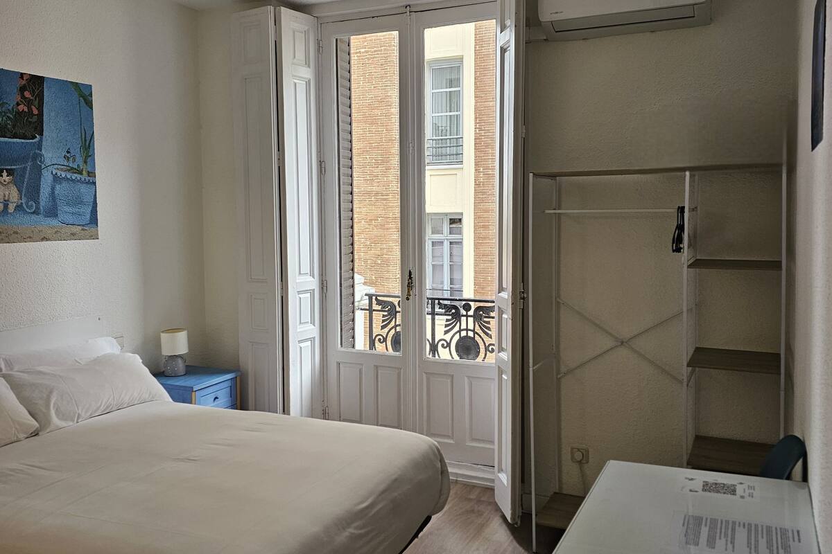 Quarto com cama, mesa de cabeceira, mesa, guarda-roupa e varanda com vista para edifícios.