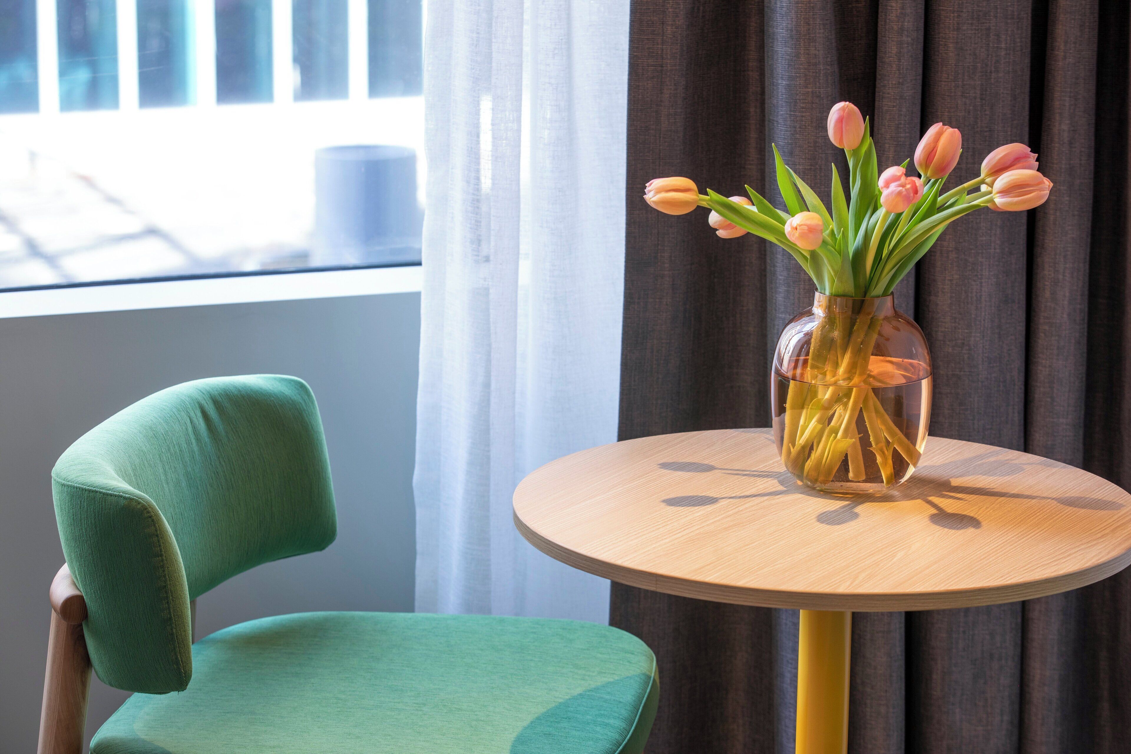 Uma cadeira verde e uma mesa redonda pequena com um vaso de tulipas cor-de-rosa.