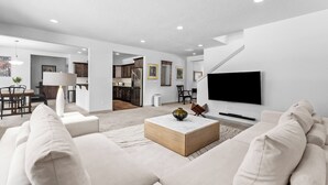 Uma sala de estar moderna com um sofá seccional grande, uma mesa de centro e uma TV de tela plana na parede.