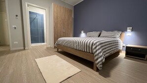 Quarto com cama, guarda-roupa de madeira, mesa de cabeceira e porta de acesso a um banheiro.