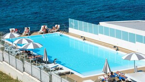 Área da piscina com espreguiçadeiras e guarda-sóis, com vista para um corpo de água.