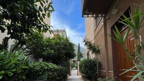 Um caminho estreito ladeado por vegetação exuberante e um edifício com entrada em azulejos.