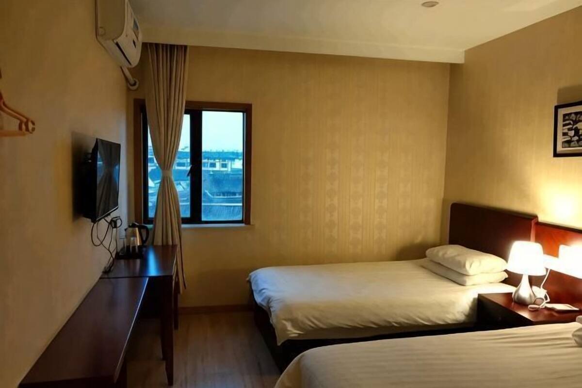 Quarto de hotel com duas camas, uma escrivaninha, uma televisão e uma janela com cortinas.