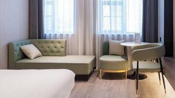 Quarto de hotel com sofá verde, mesa redonda pequena e cadeira branca.