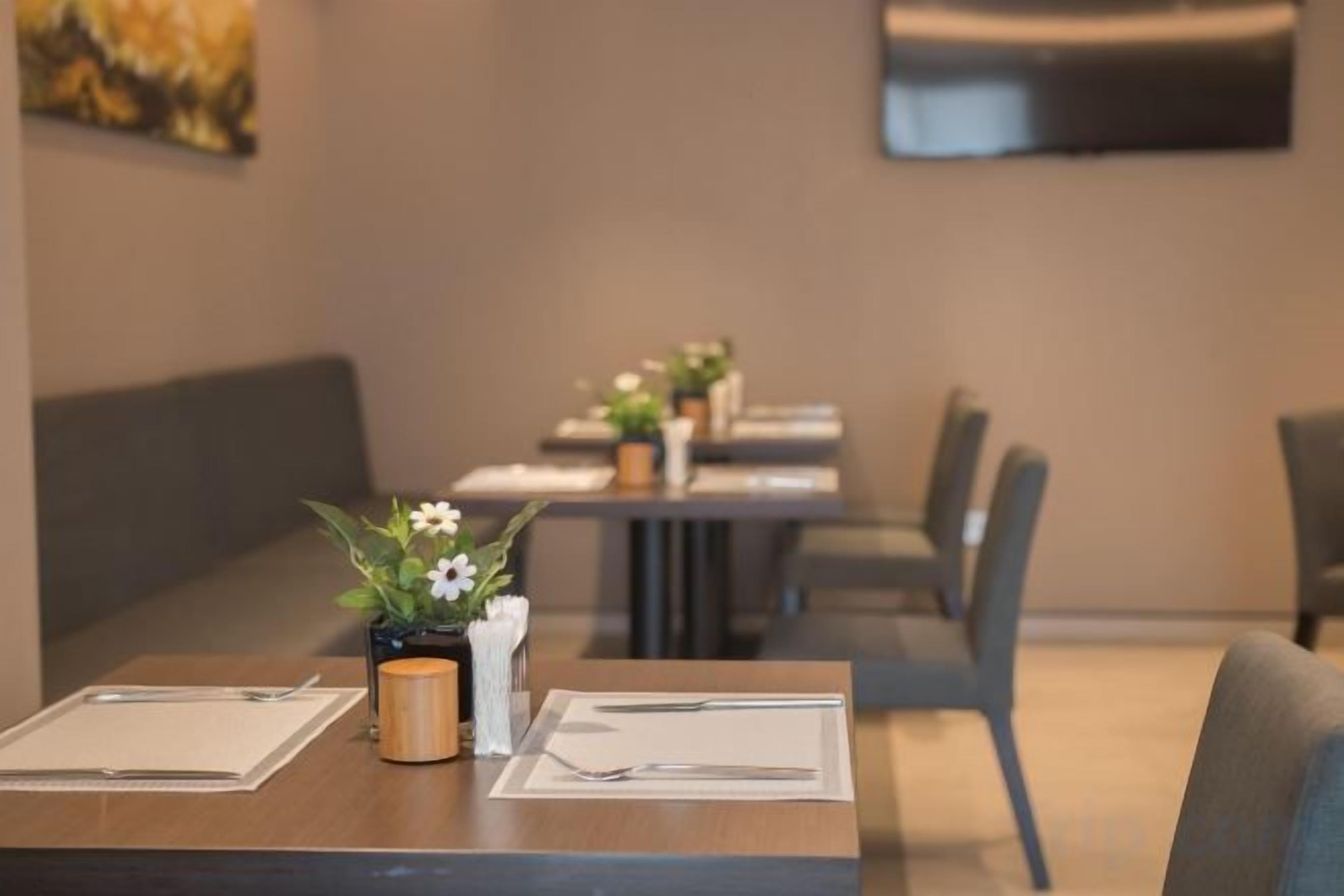 Restaurante com mesas preparadas para refeições, destacando um vaso com flores e uma vela.