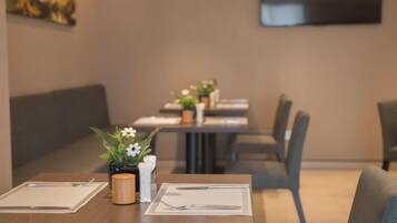 Restaurante com mesas preparadas para refeições, destacando um vaso com flores e uma vela.