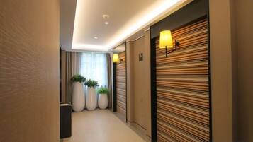 Corredor com design moderno, piso em tons claros, porta de madeira escura com ripas horizontais e luminária fixada na parede.