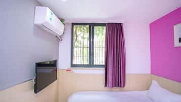 Quarto de hotel com cama, janela com cortinas, ar condicionado e televisão presa na parede.