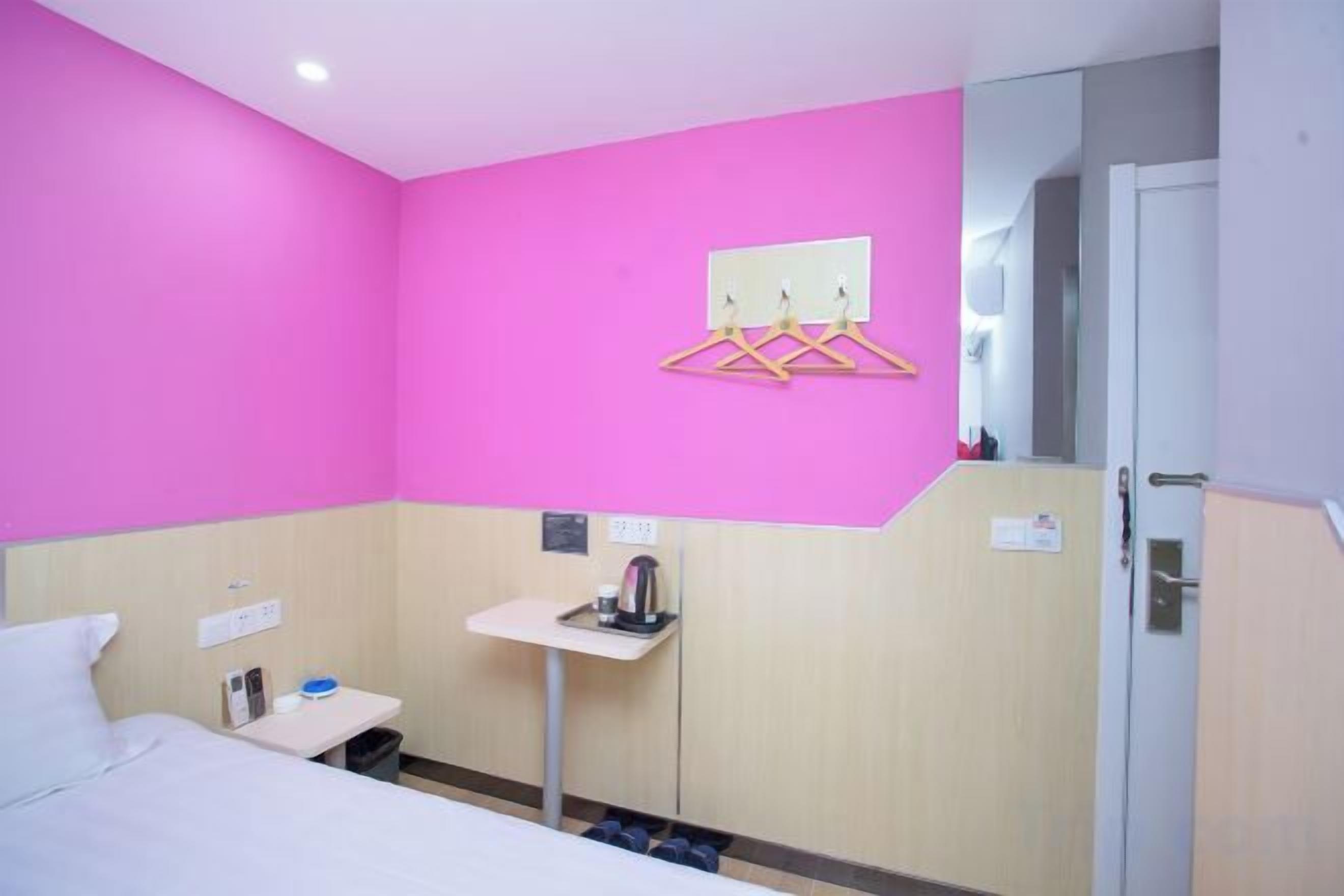 Quarto de hotel com cama, mesinha de cabeceira, espelho, luminária na parede e porta.