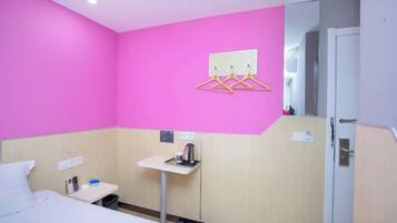 Quarto de hotel com cama, mesinha de cabeceira, espelho, luminária na parede e porta.