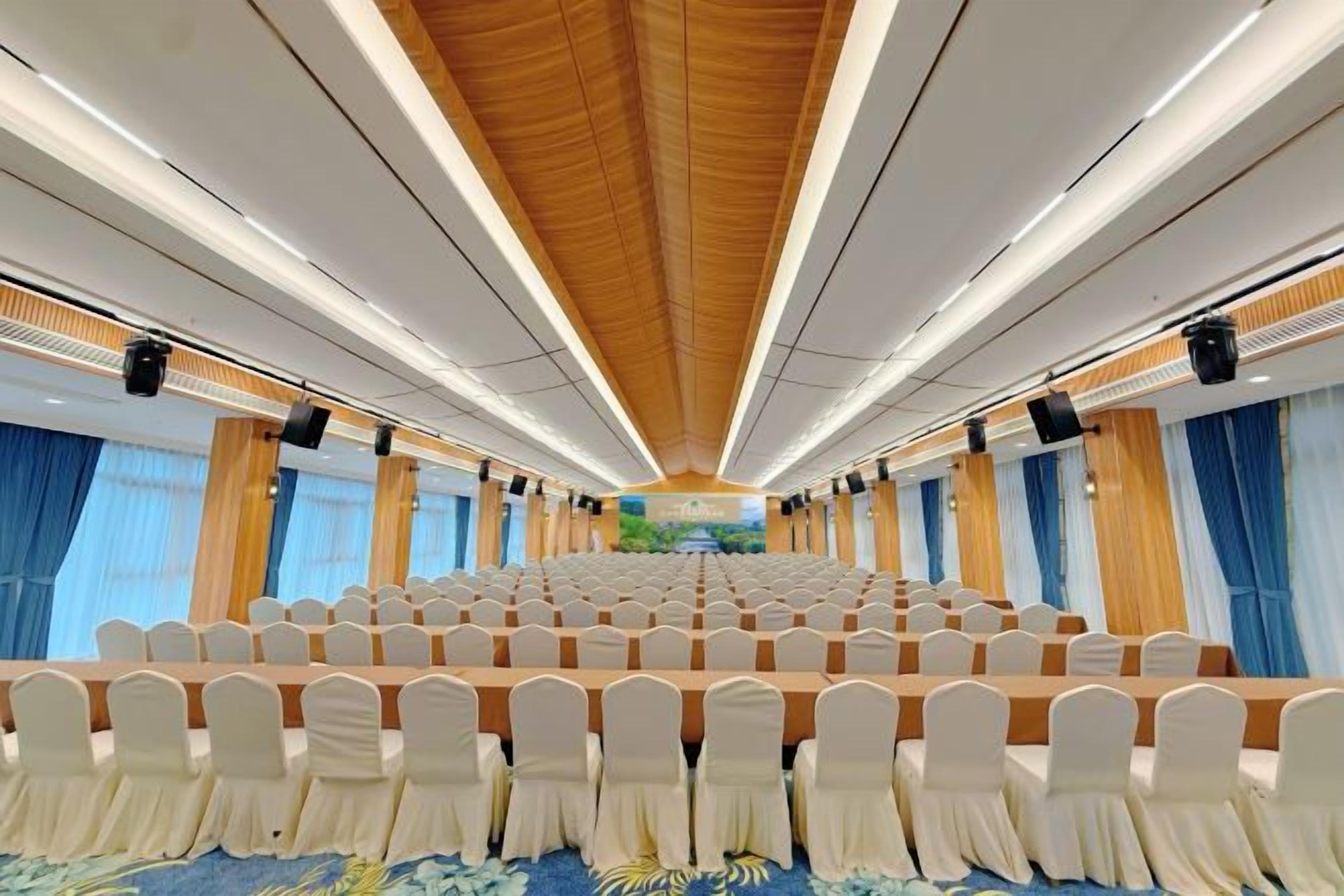 Uma sala de conferências com fileiras de cadeiras, um palco na frente e teto de madeira.