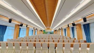 Uma sala de conferências com fileiras de cadeiras, um palco na frente e teto de madeira.