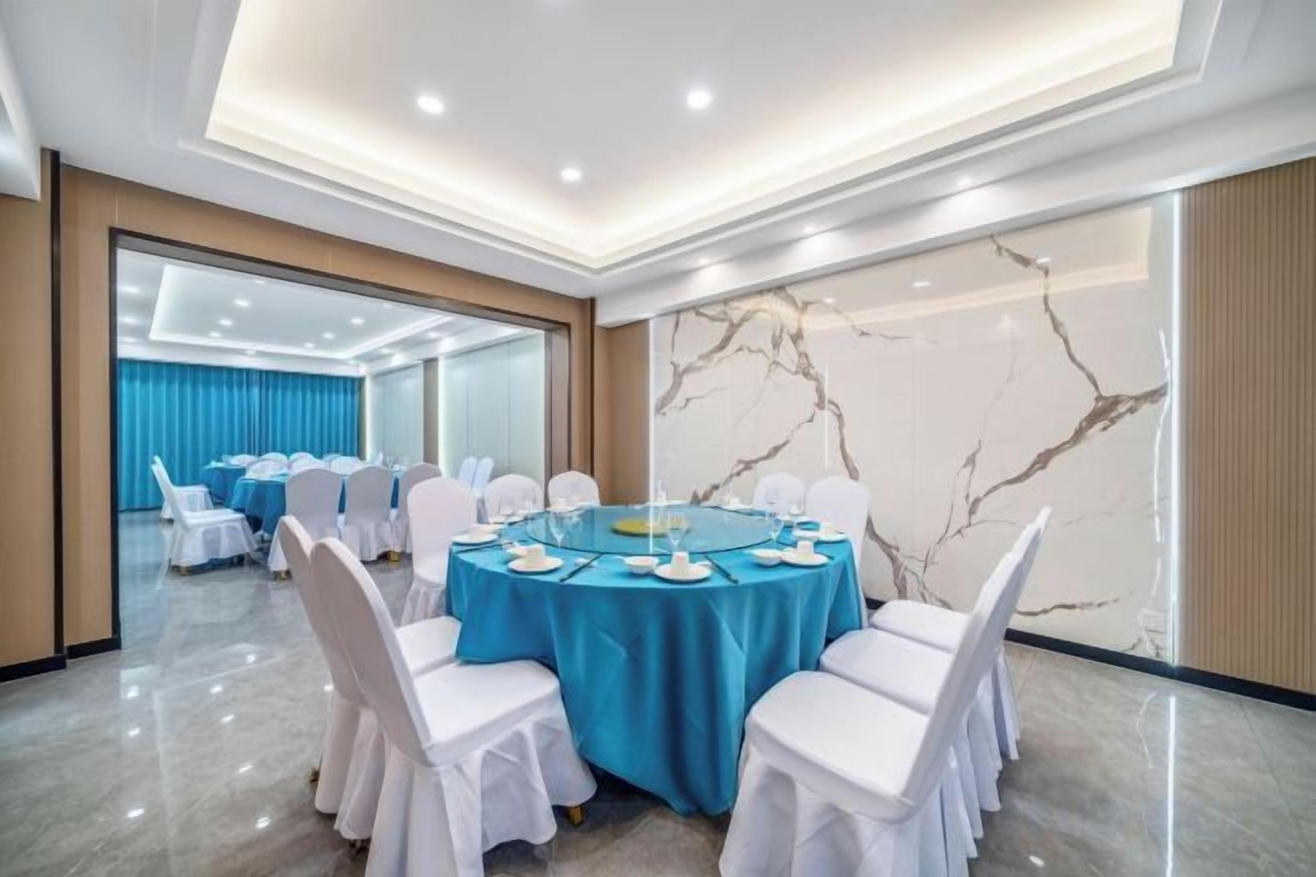 Uma sala de conferências com uma mesa redonda, cadeiras brancas e toalha de mesa azul.