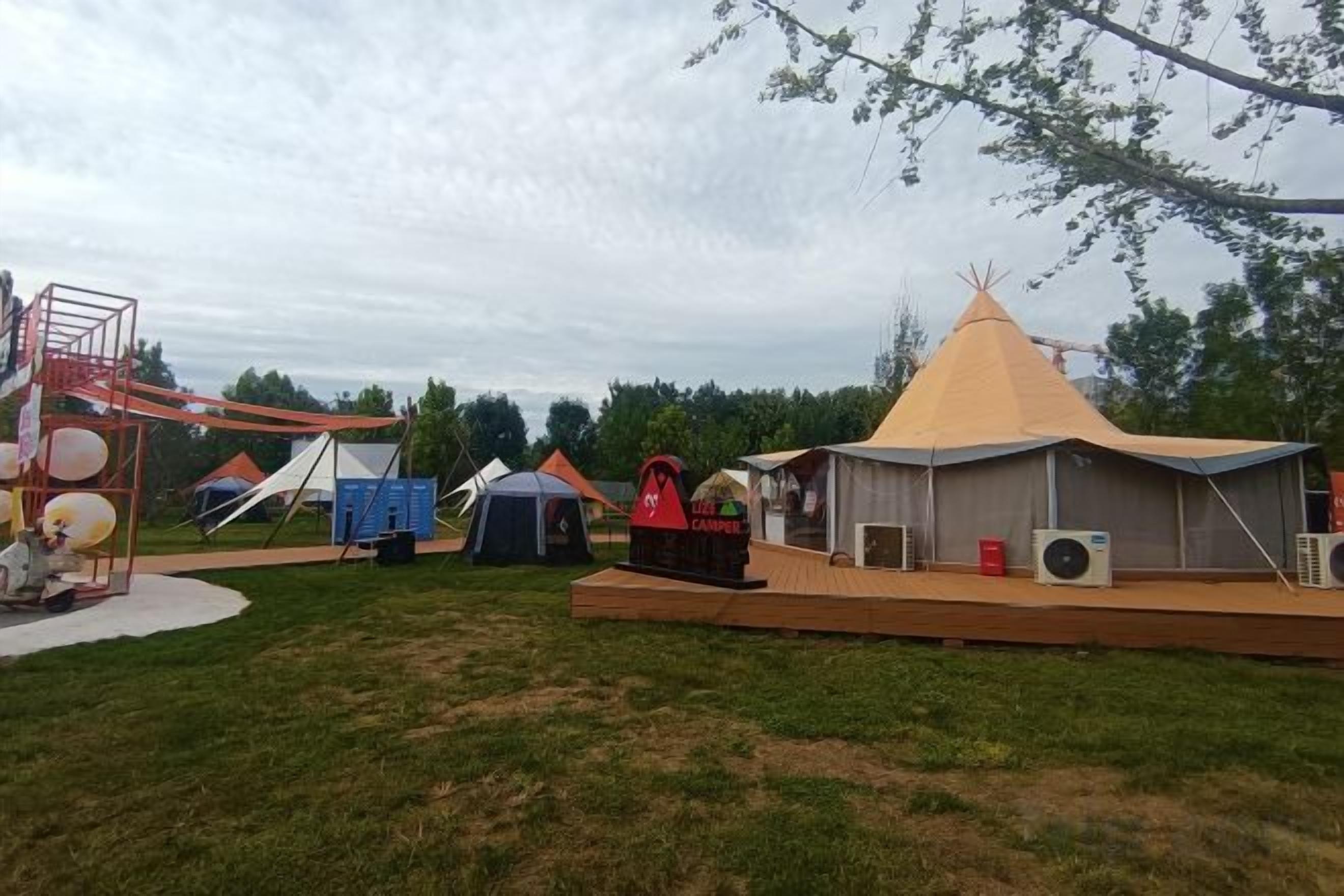 Um camping com tendas, um parquinho e um pequeno prédio com uma caixa de correio vermelha.