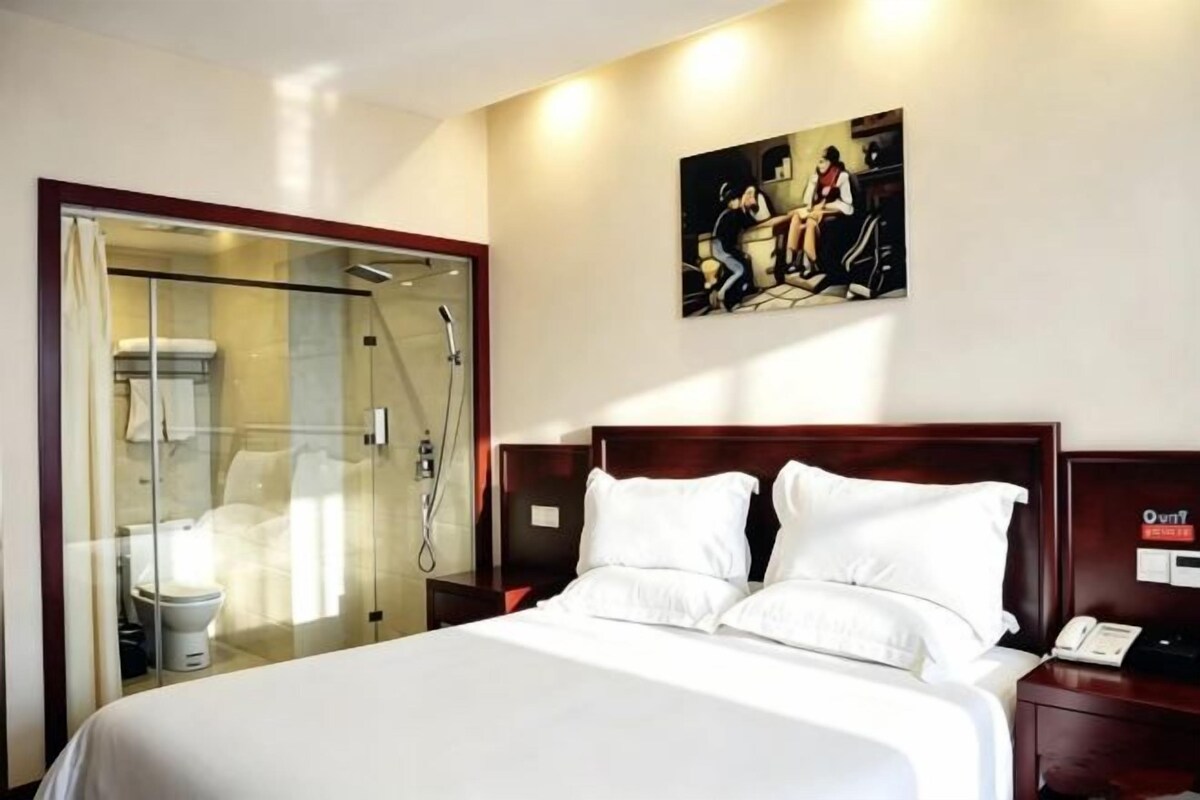 Quarto de hotel com cama, chuveiro em box de vidro e um quadro na parede.