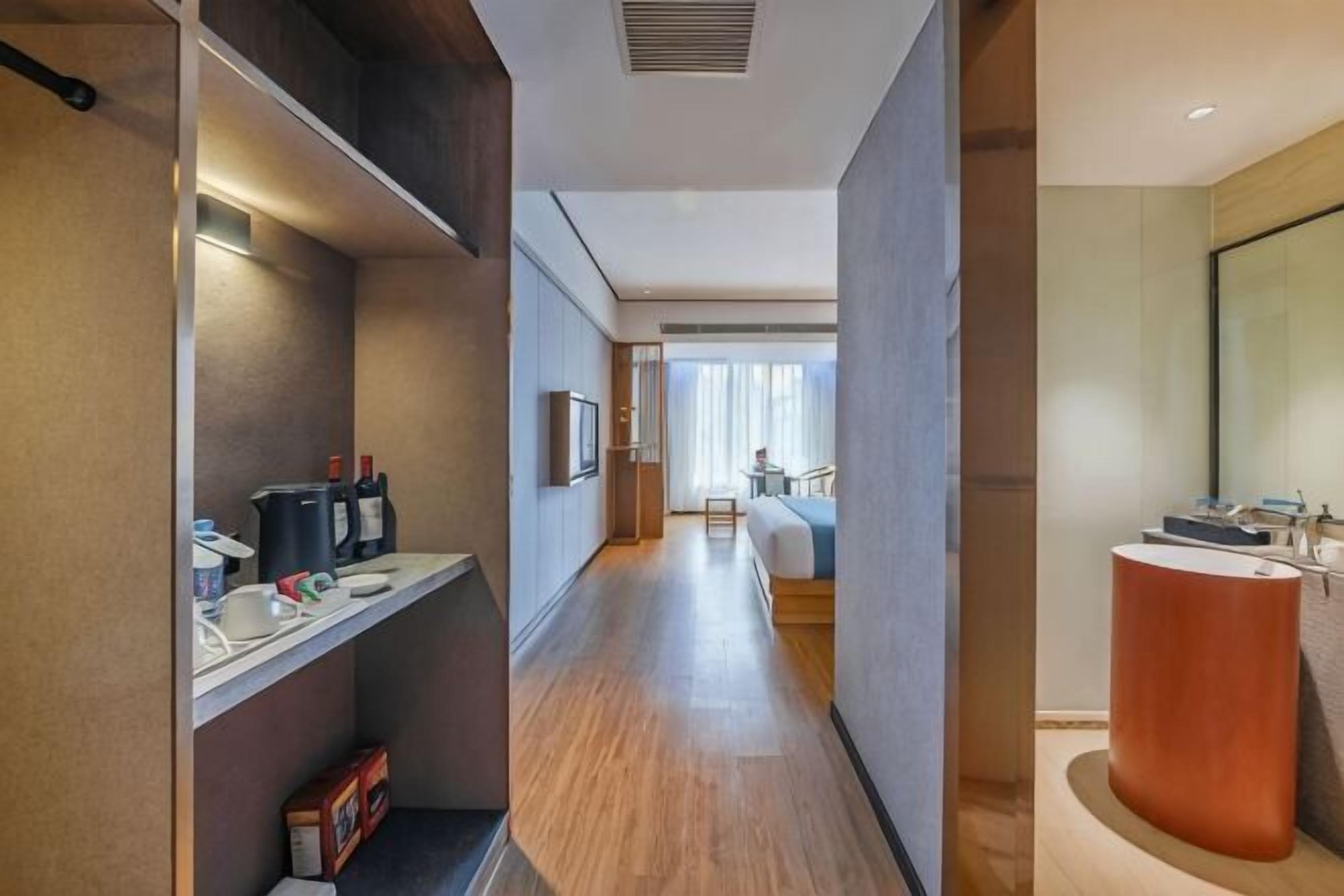 Corredor de hotel com piso de madeira, balcão de recepção, um espelho grande e um banheiro moderno com pia curva.