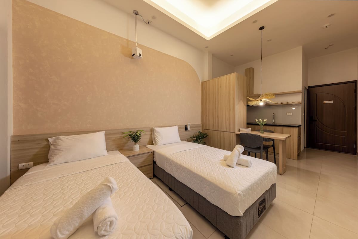 Quarto de hotel moderno com duas camas, uma kitchenette pequena e uma área de refeições.