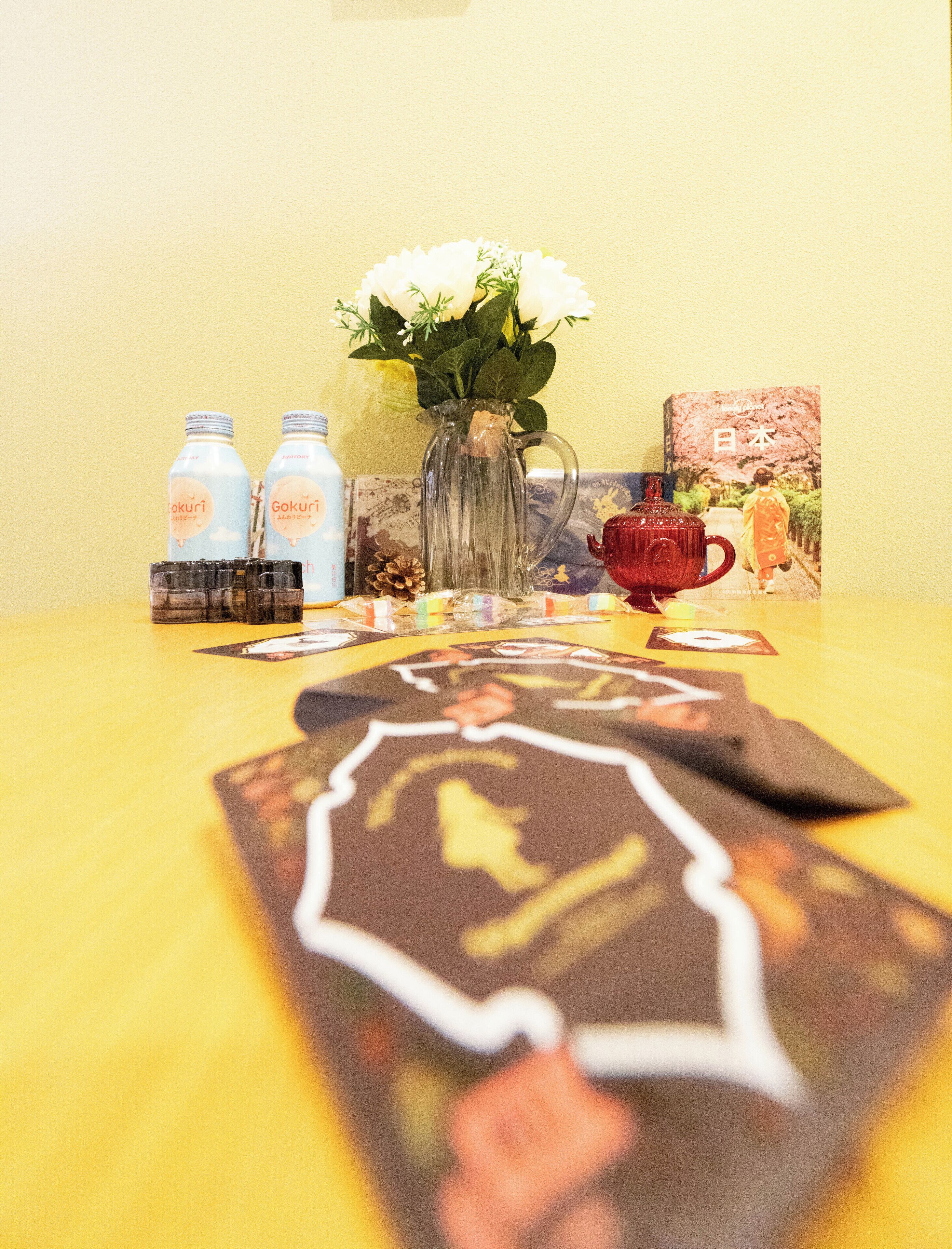 Uma mesa com um vaso de flores, duas garrafas, um bule e um jogo de cartas.
