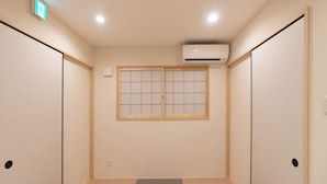 Quarto com porta deslizante, janela com padrão quadriculado, ar-condicionado e um tapete pequeno no chão.