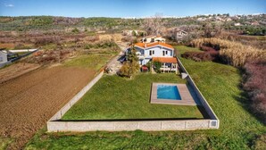Uma casa com piscina, cercada por um muro de pedra e um gramado.