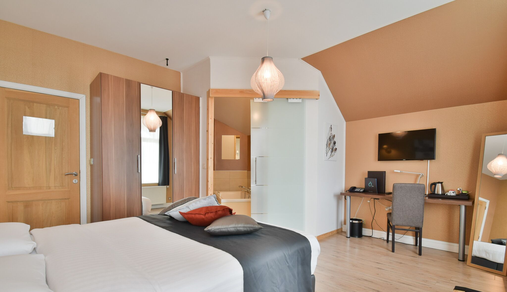 Quarto de hotel moderno com cama, escrivaninha, cadeira e televisão.