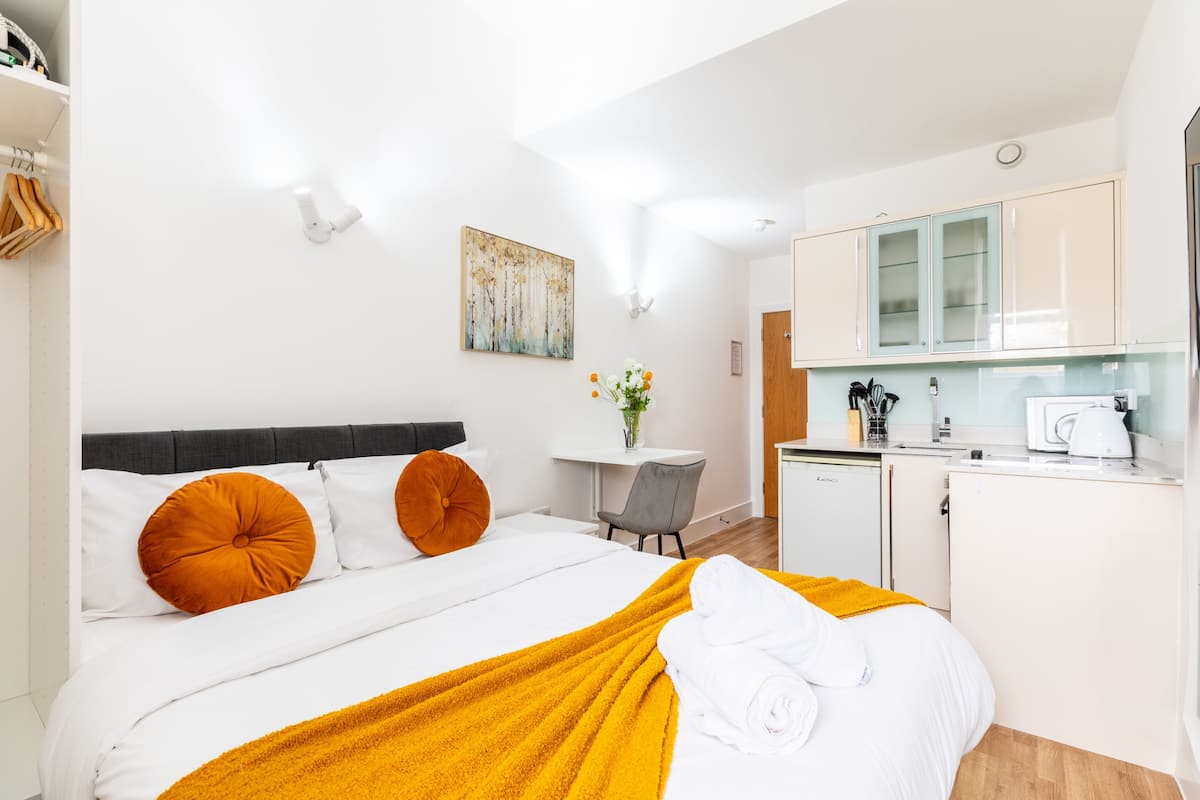 Quarto de hotel moderno com cama, escrivaninha e cozinha compacta.