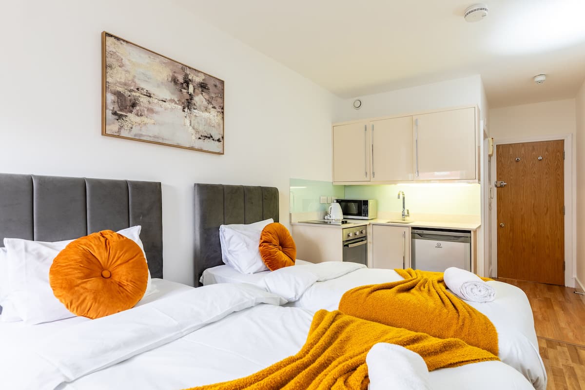 Quarto de hotel com duas camas, uma cozinha compacta e uma porta de madeira.