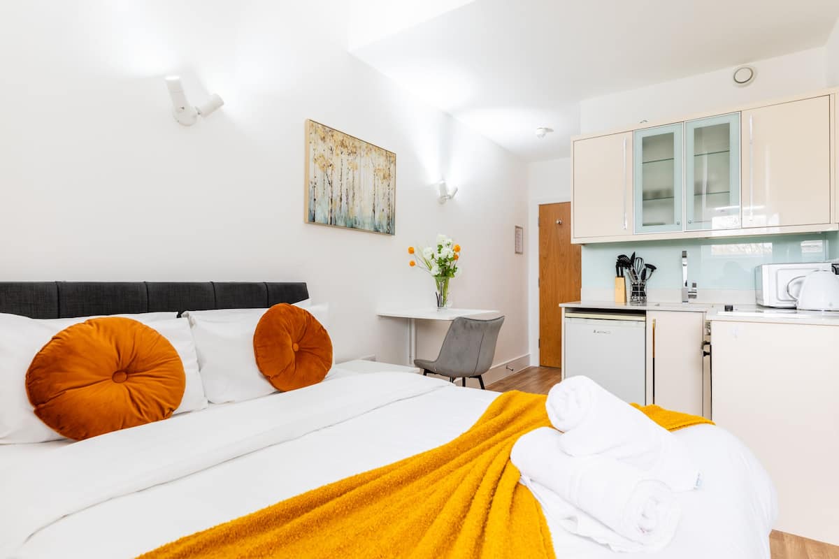 Quarto de hotel moderno com cama, secretária pequena, cozinha compacta e banheiro.
