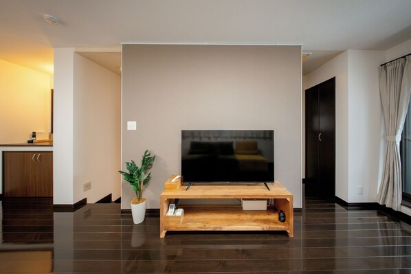 Uma sala de estar moderna com uma televisão de tela plana sobre um suporte de madeira, uma planta em vaso e um piso de madeira escura.