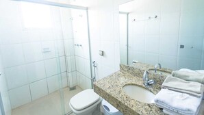 Casa de banho moderna com cabine de duche em vidro, lavatório com bancada de granito e um espelho grande.
