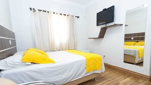 Quarto de hotel com uma cama, televisão, espelho e chão de madeira.