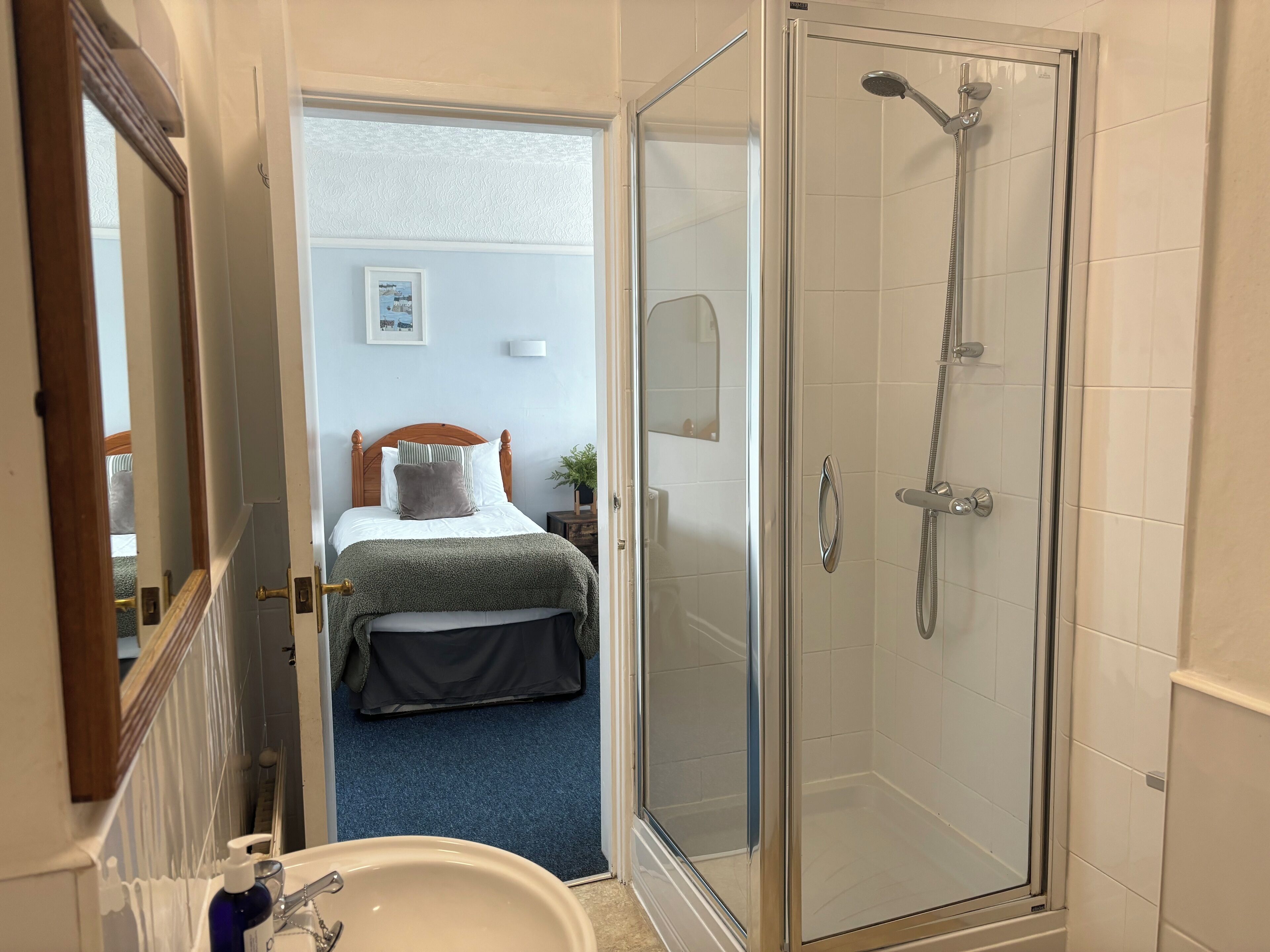 Casa de banho de hotel com chuveiro, pia e cama com vista para o corredor.