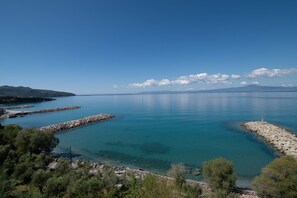 Vista costeira com águas azul-claras, paredões rochosos e montanhas ao longe.